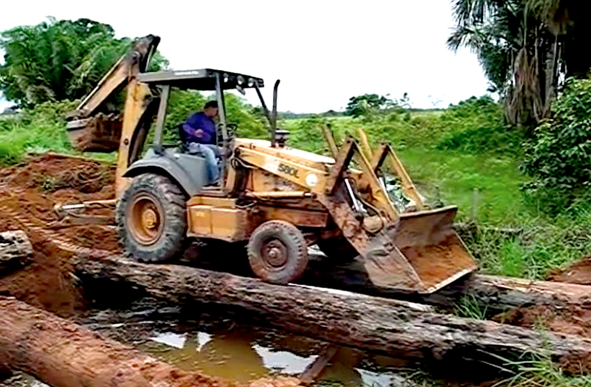 Backhoe shimmies across water on a bridge made of old logs | Equipment ...